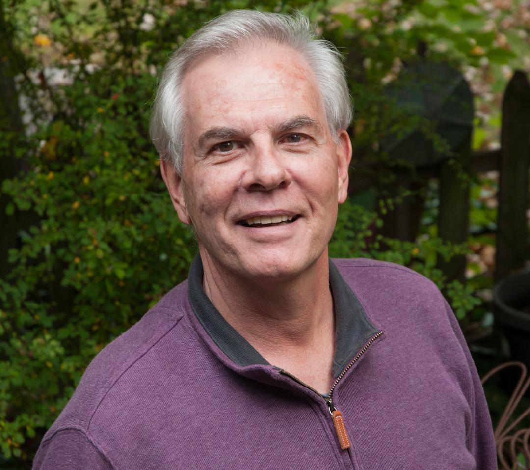 Smiling man outdoors in a purple sweater. - Faulkner Society